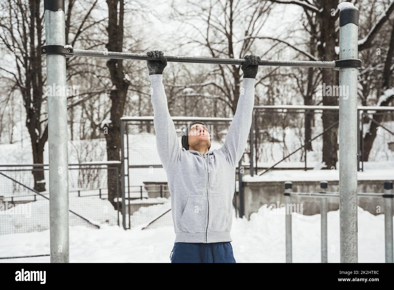 Athletic man doing pull-ups on horizontal bar during his outdoor winter ...