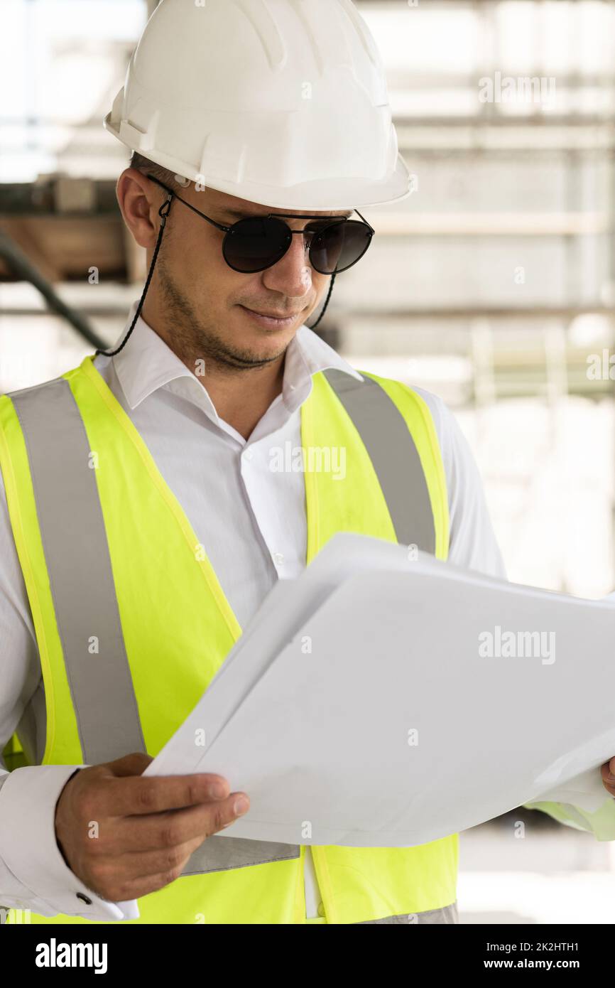 Man architect wearing safety vest with a blueprints on a construction ...