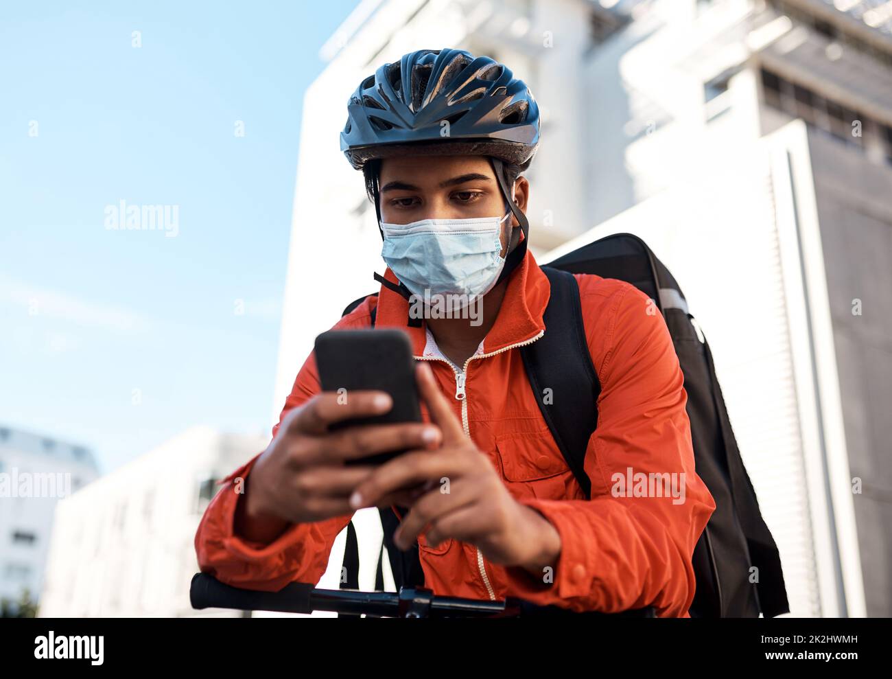 Managing his deliveries with his smartphone. Shot of a masked man using ...