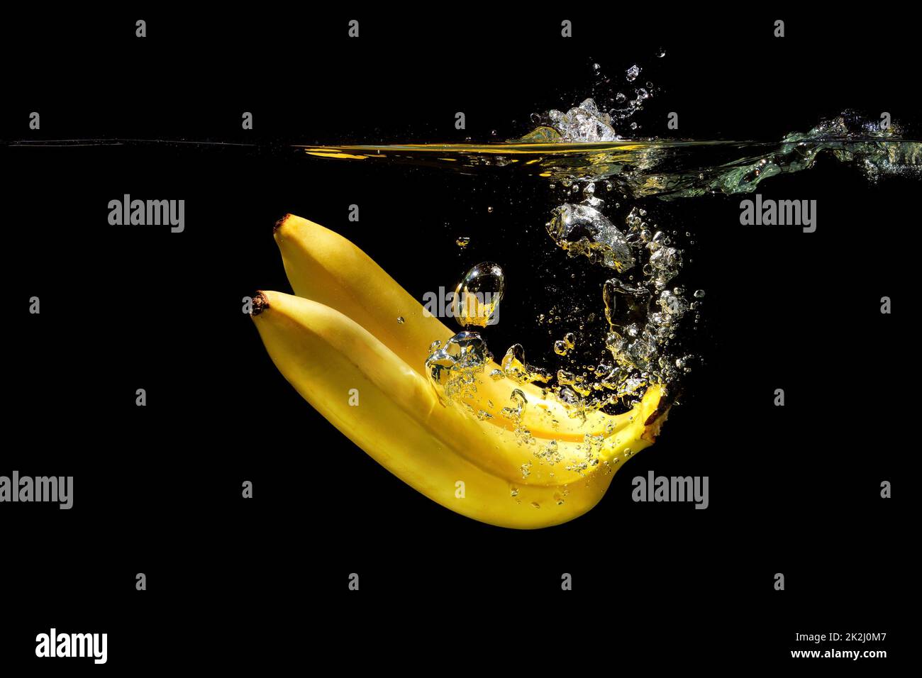 Two ripe yellow bananas dropped in water isolated on black background ...