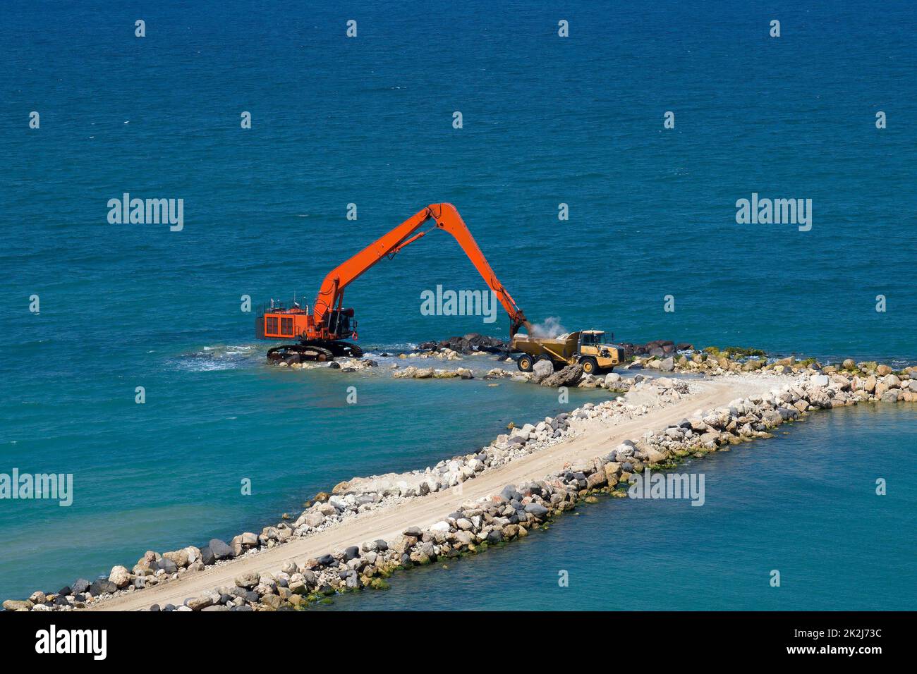 An excavator and a mining truck move stones into the sea. Construction ...