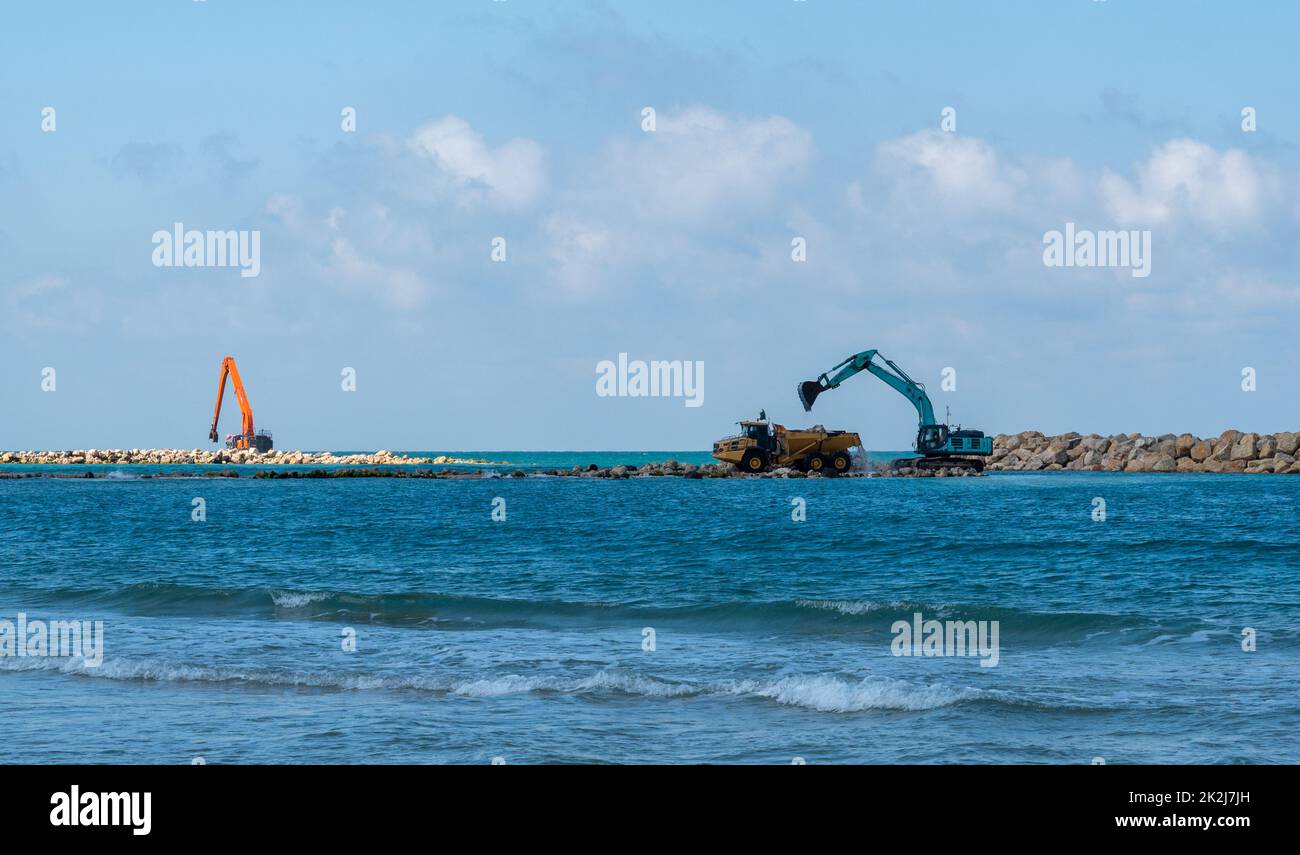 An excavator and a mining truck move stones into the sea. Construction ...
