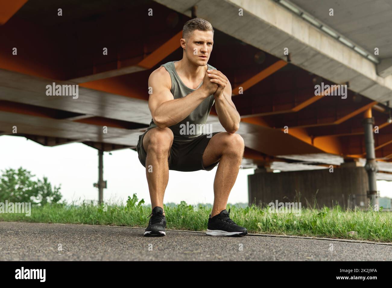 Muscular man is making squats under the bridge during his street ...