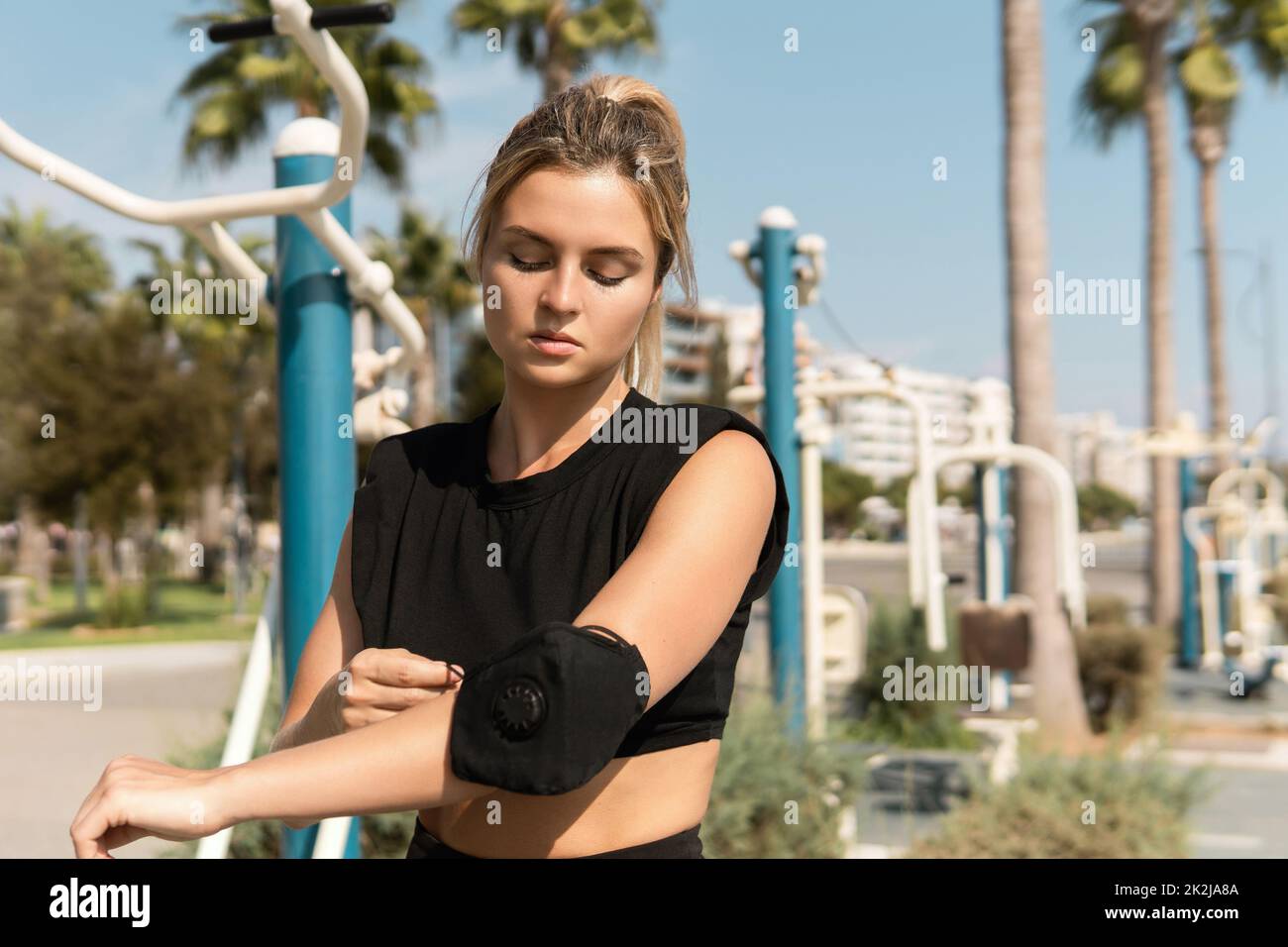 Athletic woman wearing face mask on her elbow during summer street ...