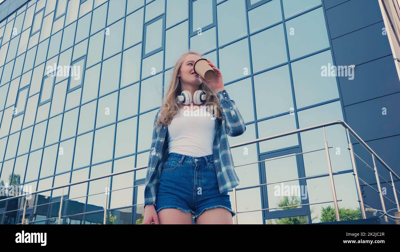 Low angle view of smiling young woman with headphones holding takeaway ...