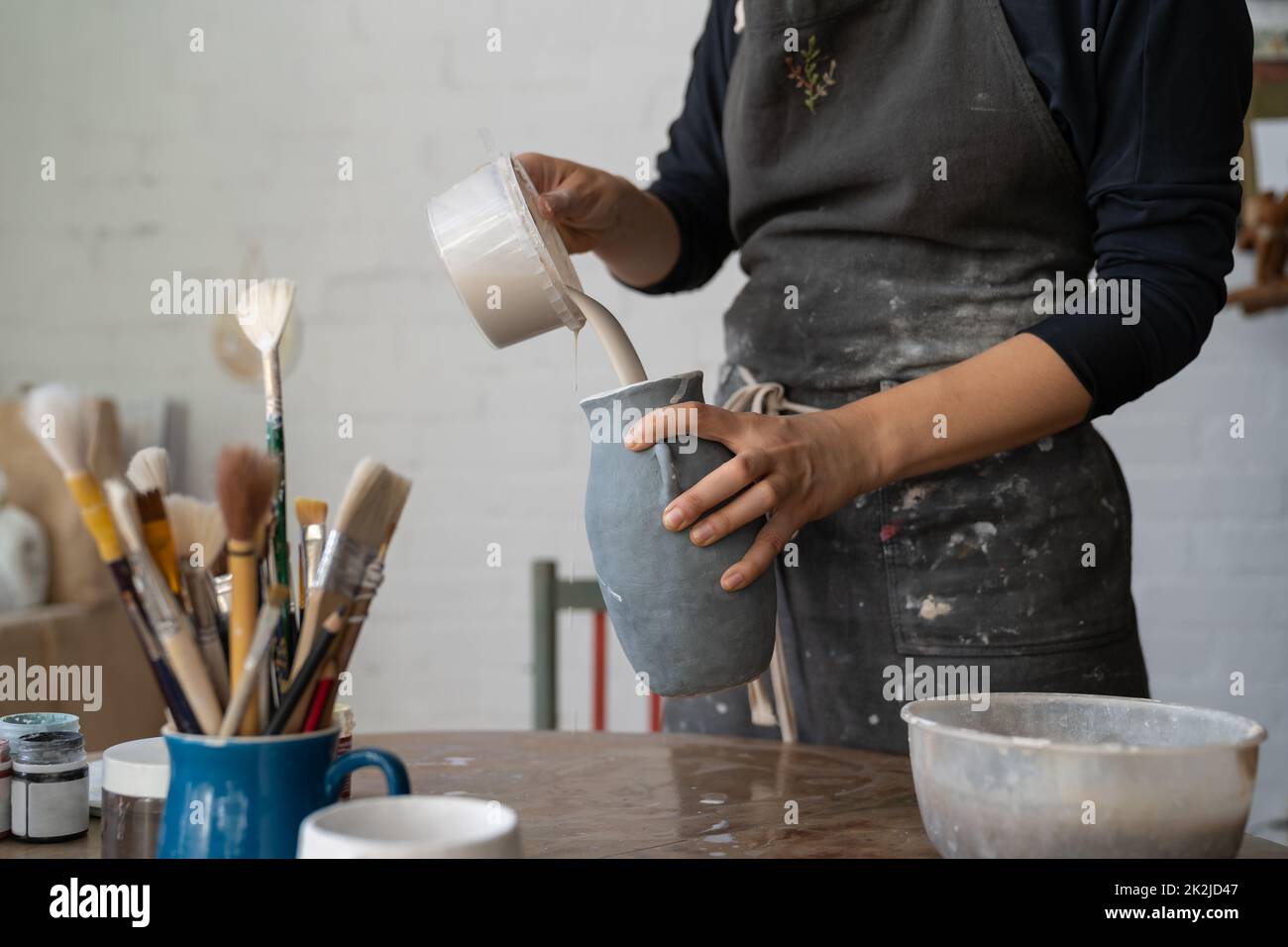 Craftsmaster in apron pours liquid from plastic bowl into grey vase to ...