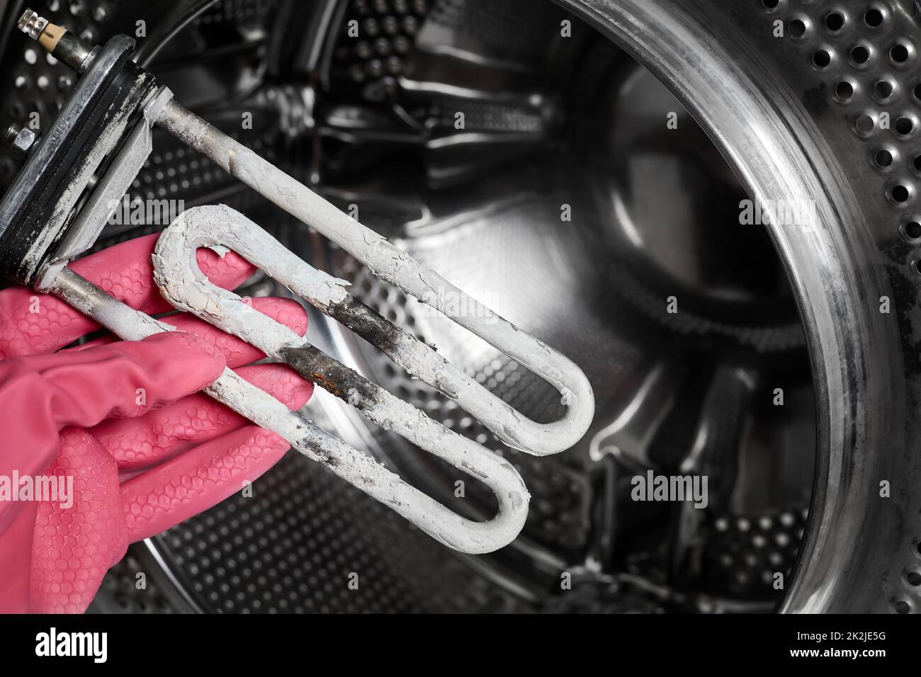 A man holds in his hand a burnt-out heating element of a washing ...