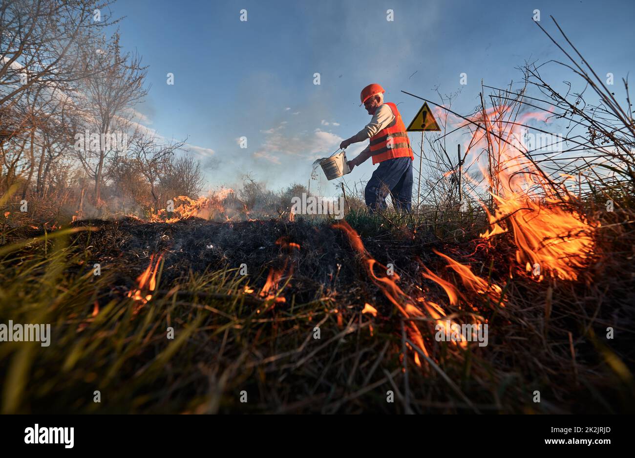 Firefighter ecologist extinguishing fire in field with evening sky on ...