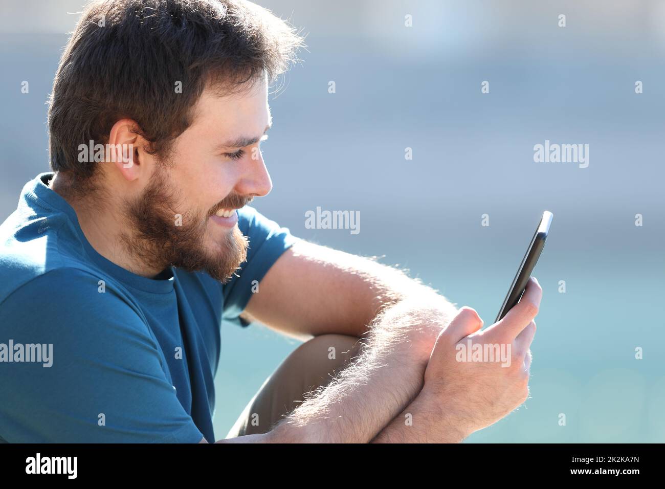 Happy man using mobile phone sitting outdoors Stock Photo - Alamy