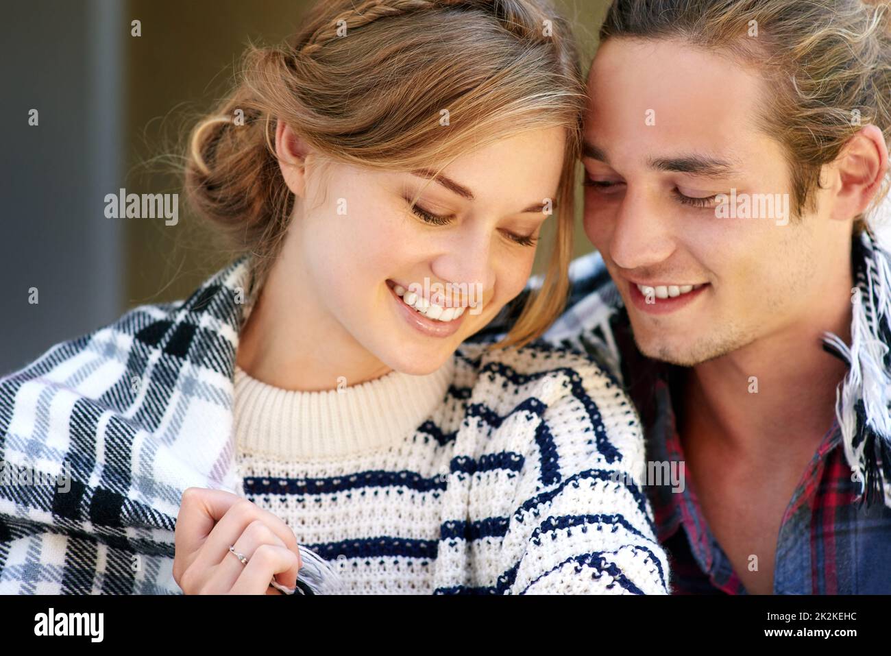 Cozying up for winter. a young couple wrapped in a blanket together ...