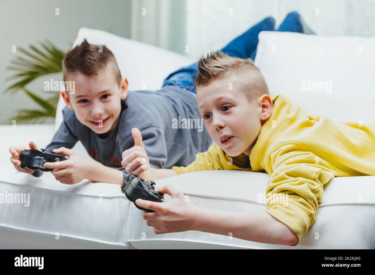 Two young brothers playing video games together on the couch Stock ...