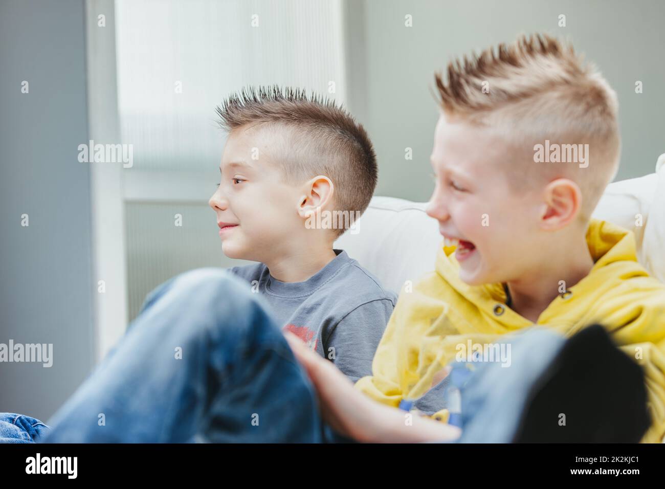 Young boy sitting on a sofa with his laughing brother Stock Photo - Alamy