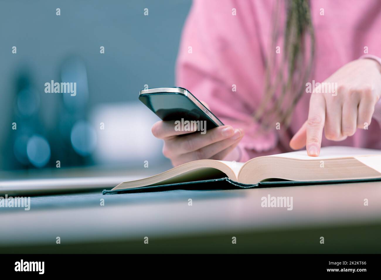 Woman holding mobile phone while reading book Stock Photo - Alamy