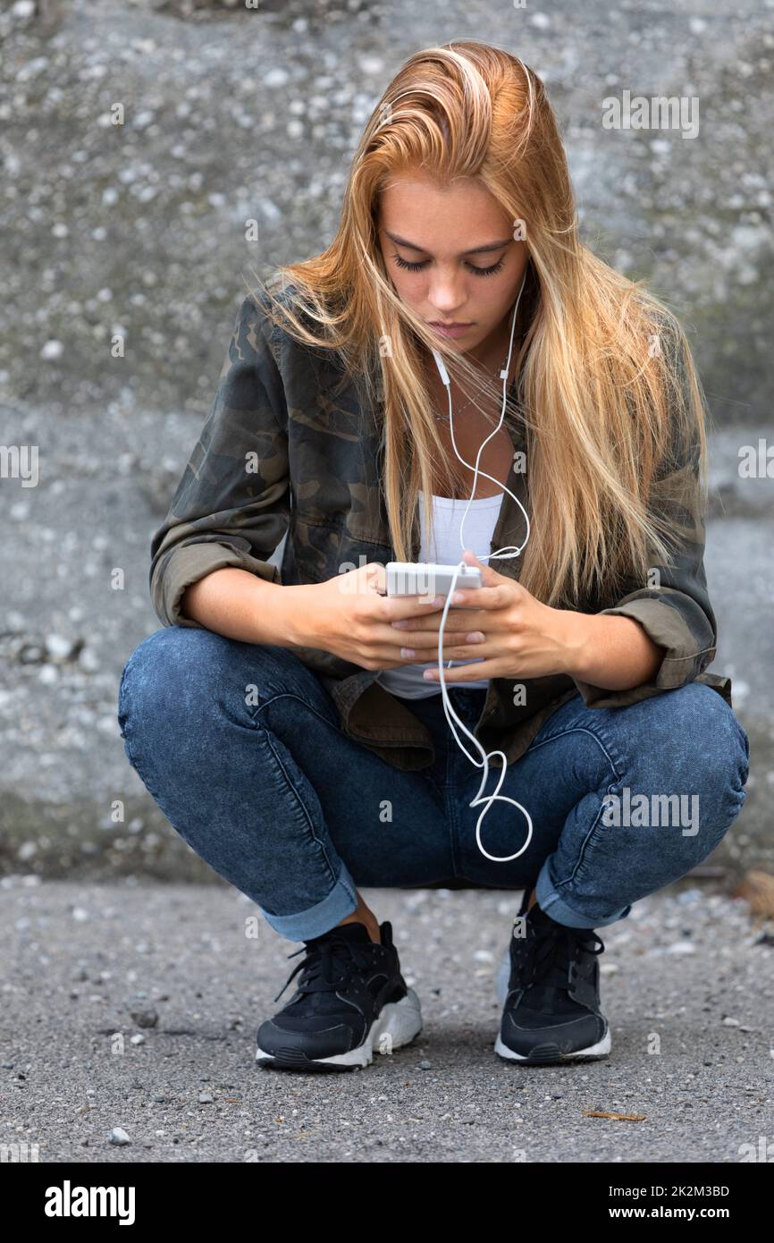 Young woman crouching down listening to music Stock Photo - Alamy