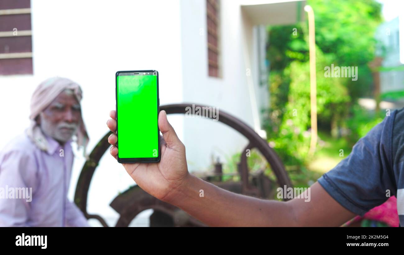 Young Asian man showing a green screen cell phone with rural village ...