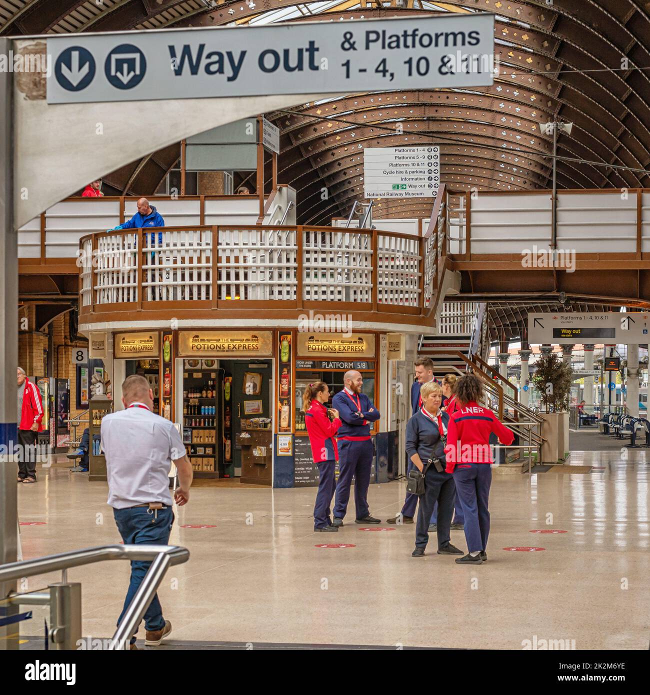 A railway station crew stand in a group talking on a concourse. A kiosk ...