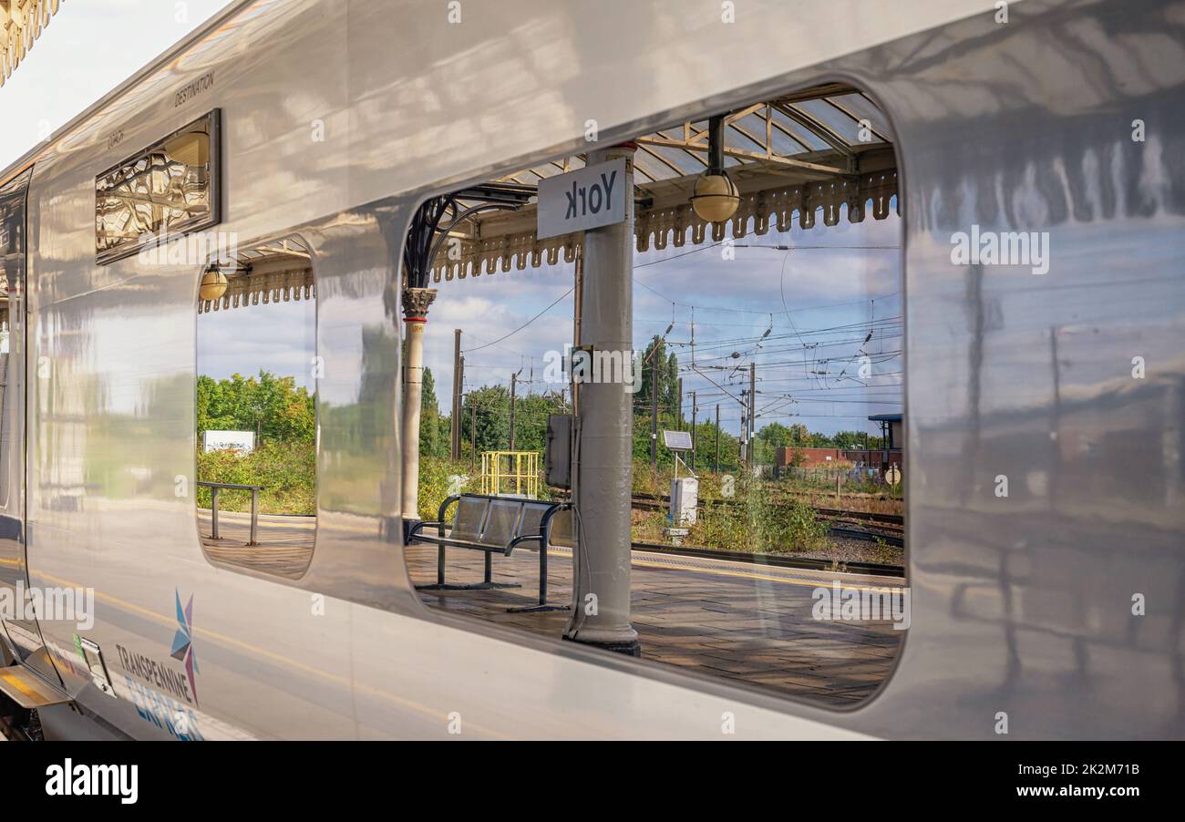 A railway station bench and column with a place name is reflected in ...