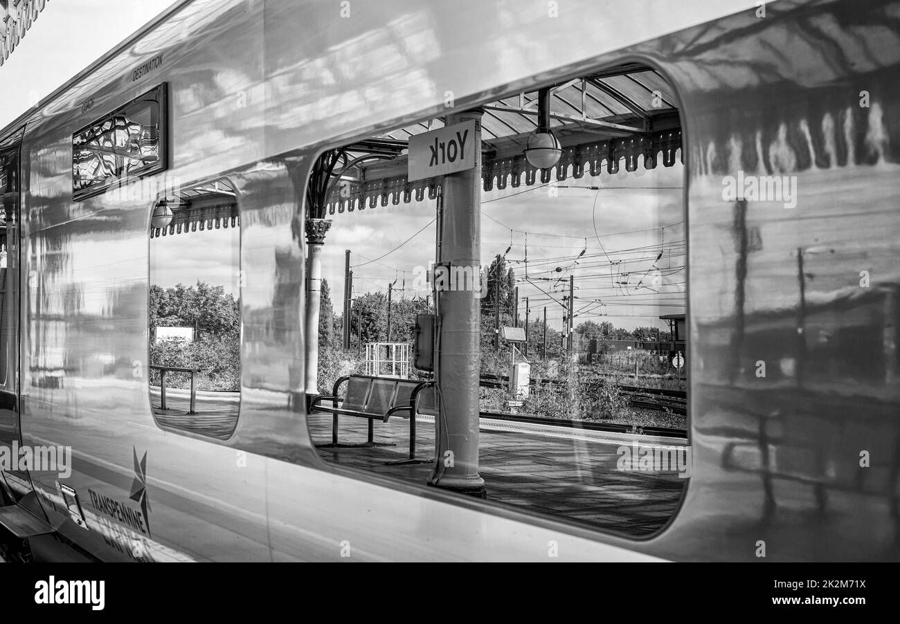 A railway station bench and column with a place name is reflected in ...