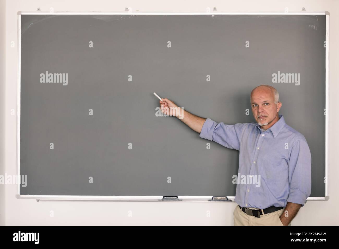 Senior teach holding chalk pointing to chalkboard Stock Photo - Alamy