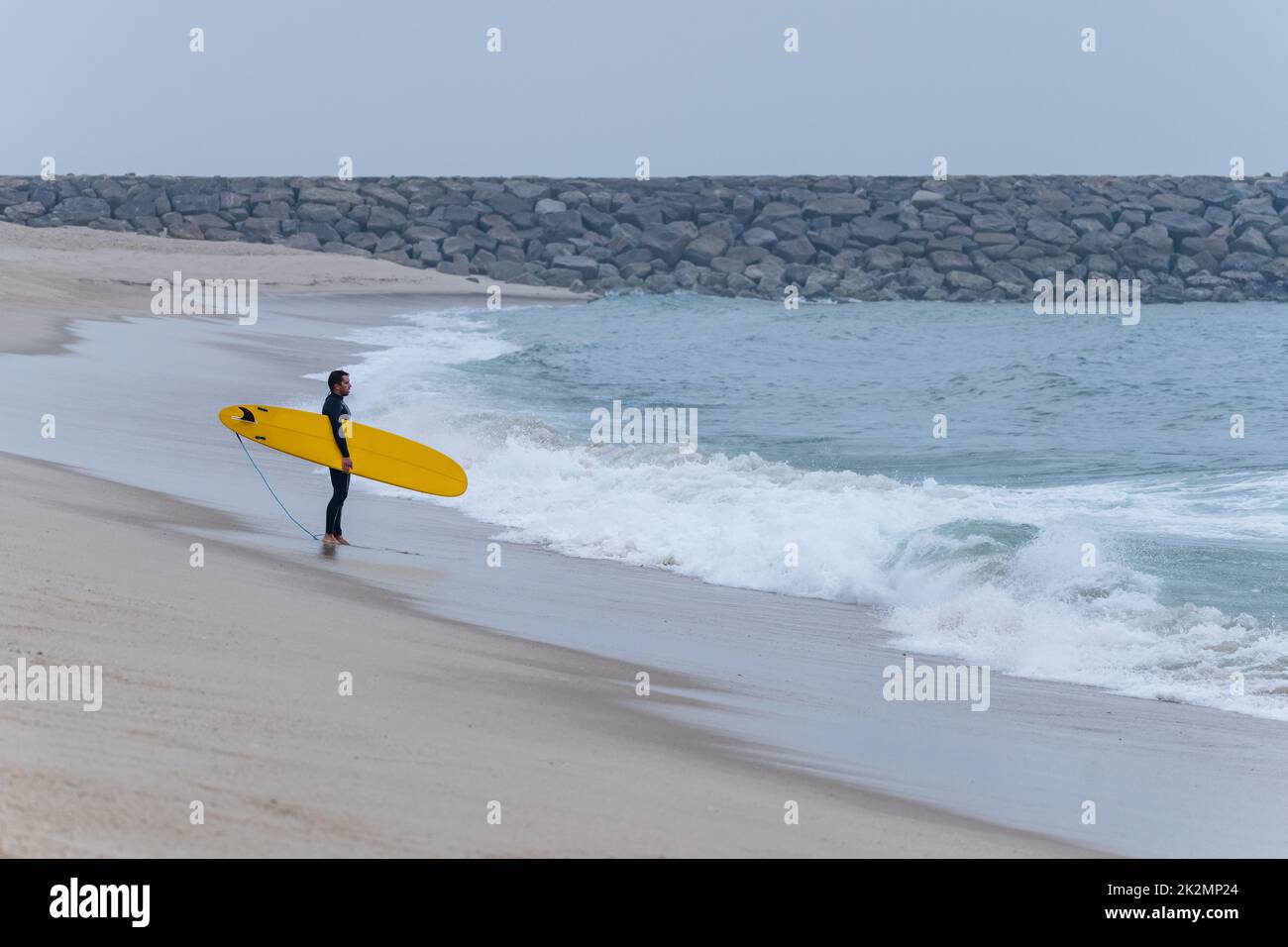 Surfer with board under his arm on a cloudy morning at Furadouro beach ...