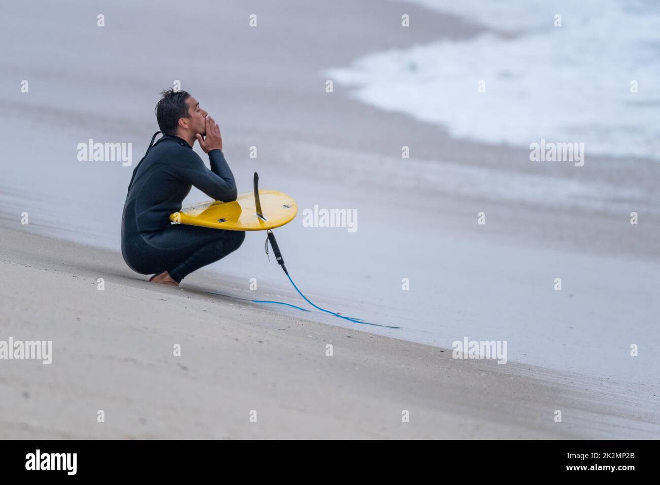 Surfer crouching with his board looking at the sea with his hands on ...