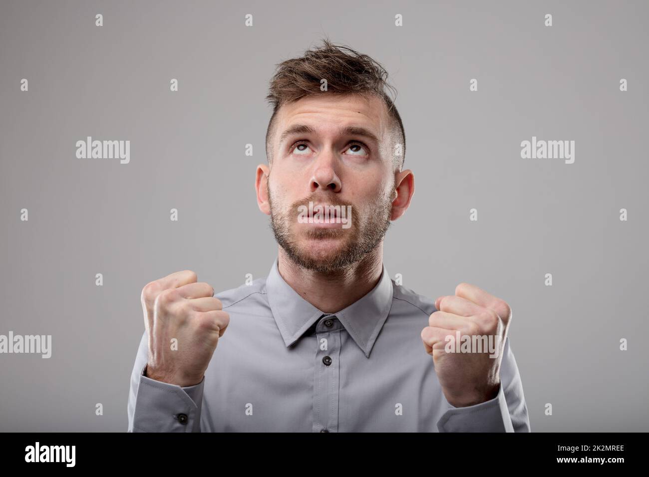 Intense bearded young man clenching his fists as he stares up into the ...