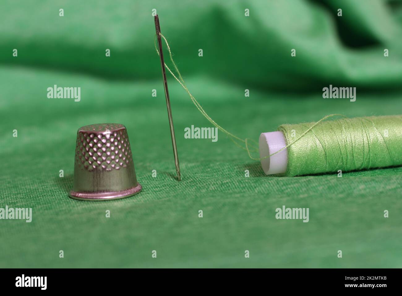 Spool of Green Thread, Thimble and Needle on Green Fabric Stock Photo ...