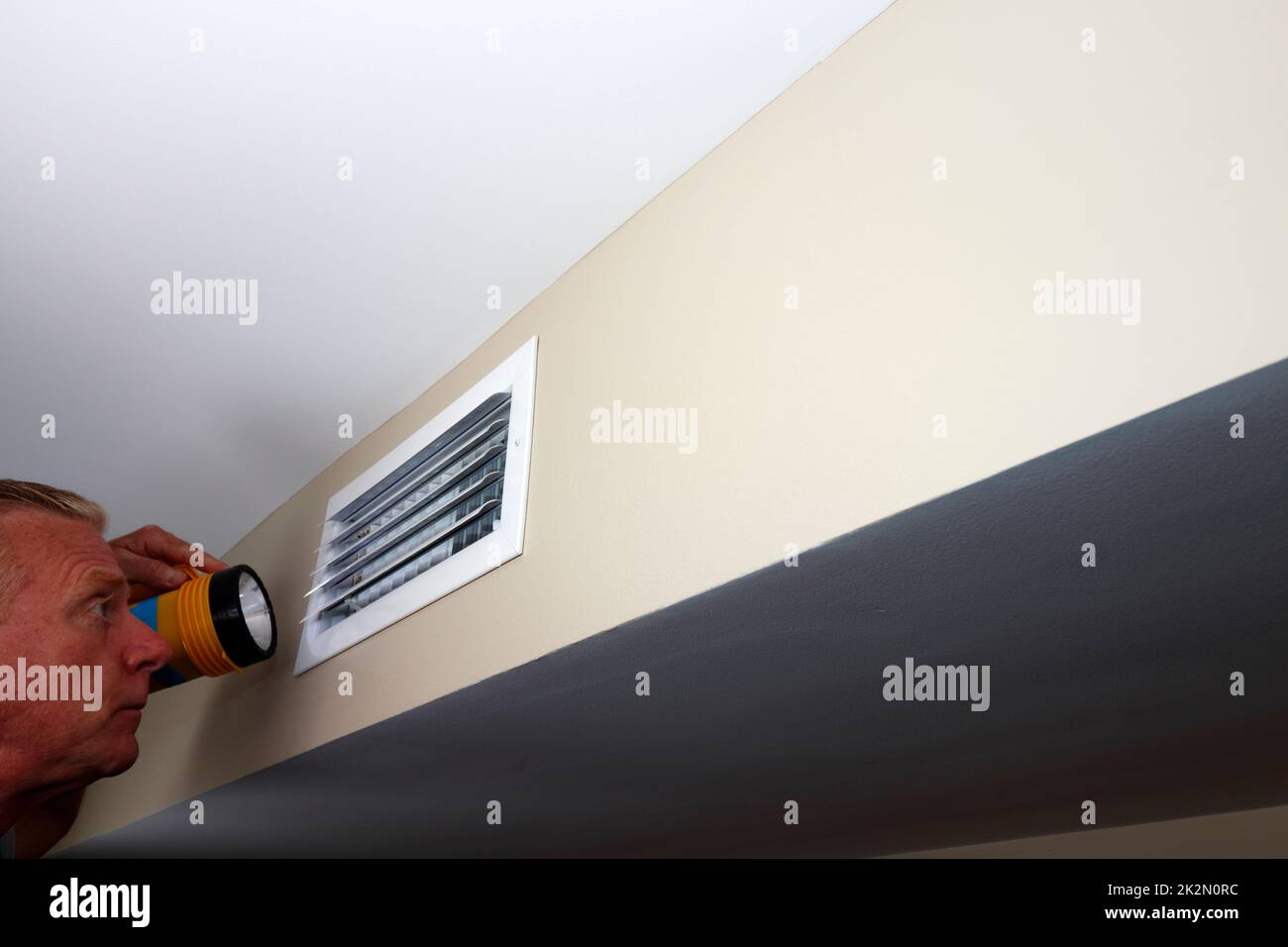 Man Looking into a Rectangle Home Wall Vent with a Flashlight Stock ...