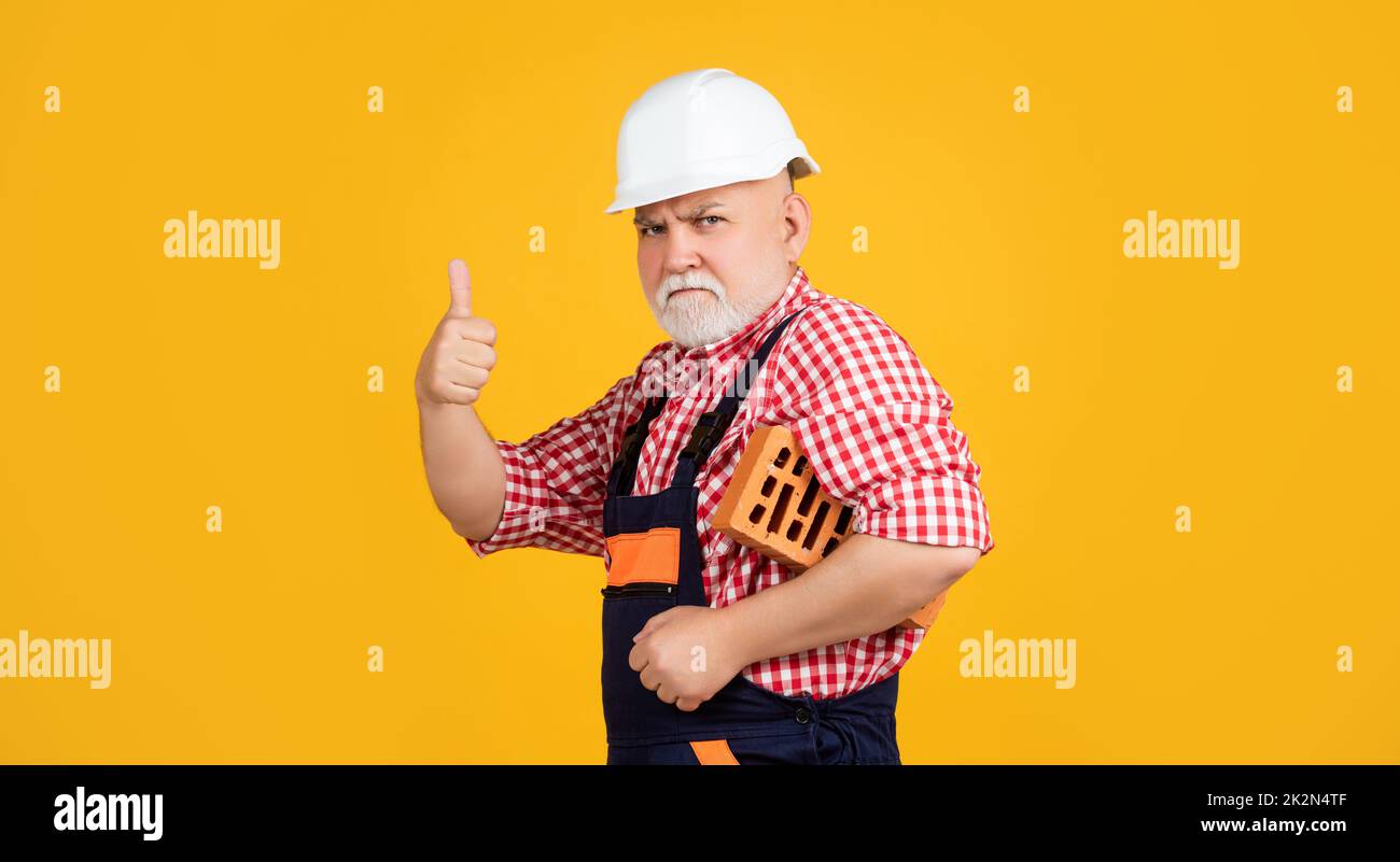 serious old aged man bricklayer in helmet on yellow background Stock ...