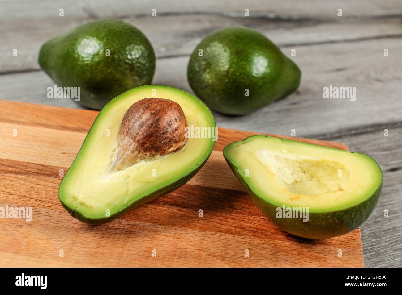 Avocado cut in half, seed visible, on wooden chopping board, two more ...