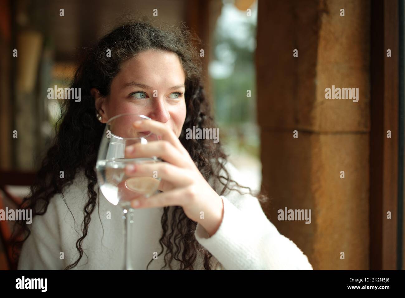 Happy woman holding glass of water looks through window Stock Photo - Alamy