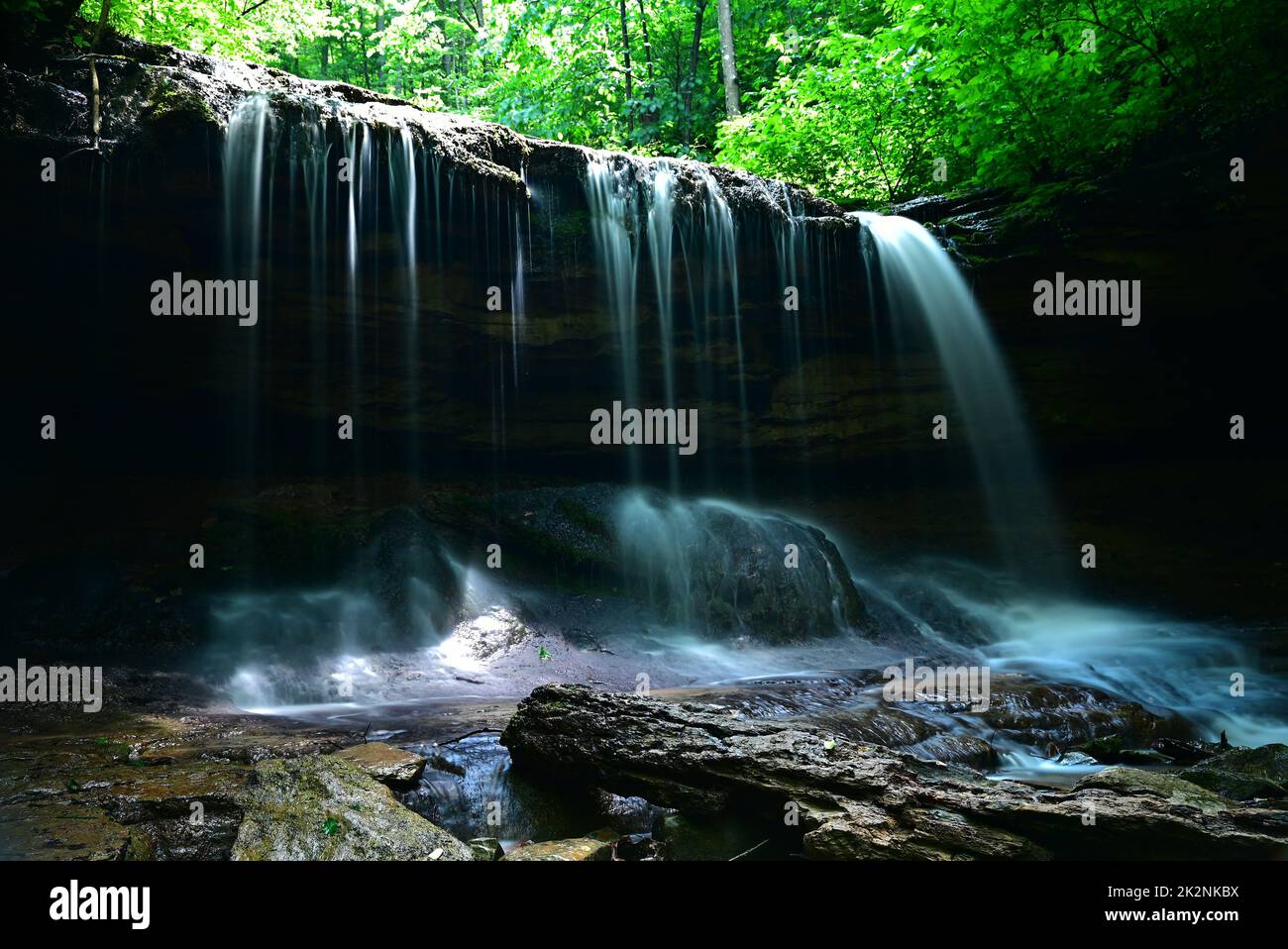 A waterfall falling from rocks surrounded by green trees Stock Photo ...