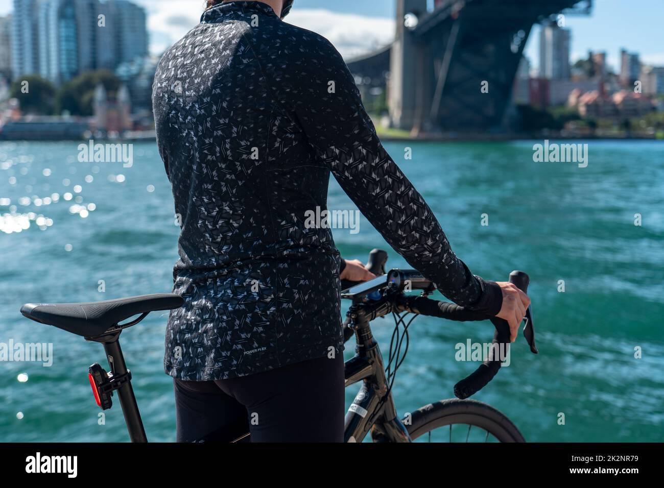 A bike rider holding bike steering wheel and standing in front of water ...