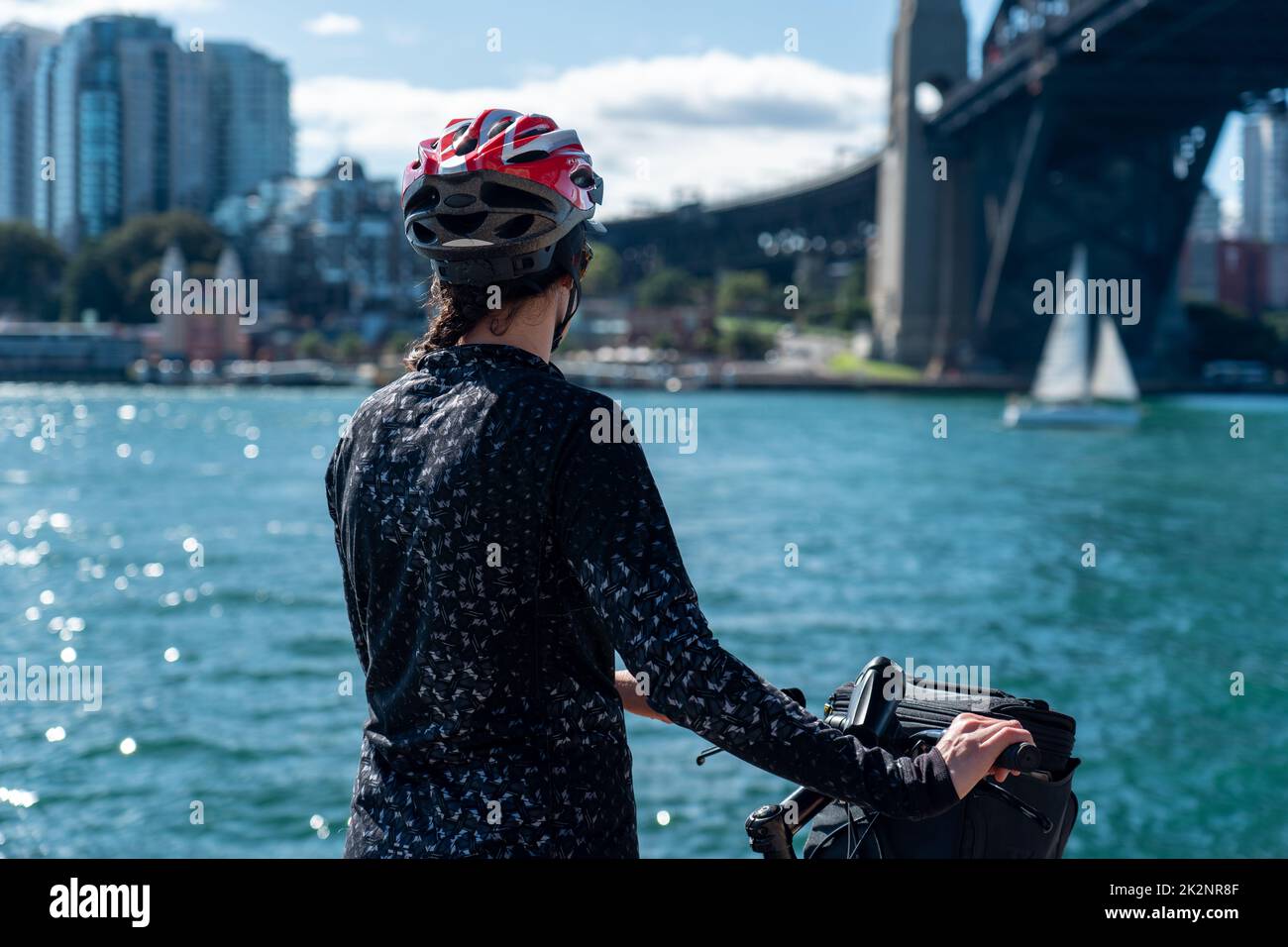 A bike rider holding bike steering wheel and standing in front of water ...