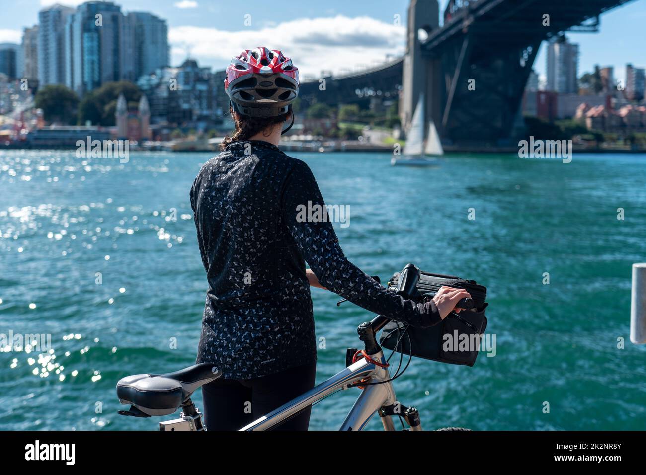 A bike rider holding bike steering wheel and standing in front of water ...