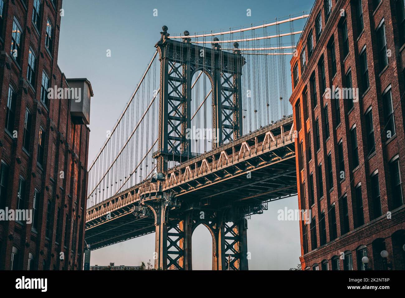 The famous Brooklyn Bridge between two buildings against the blue sky ...