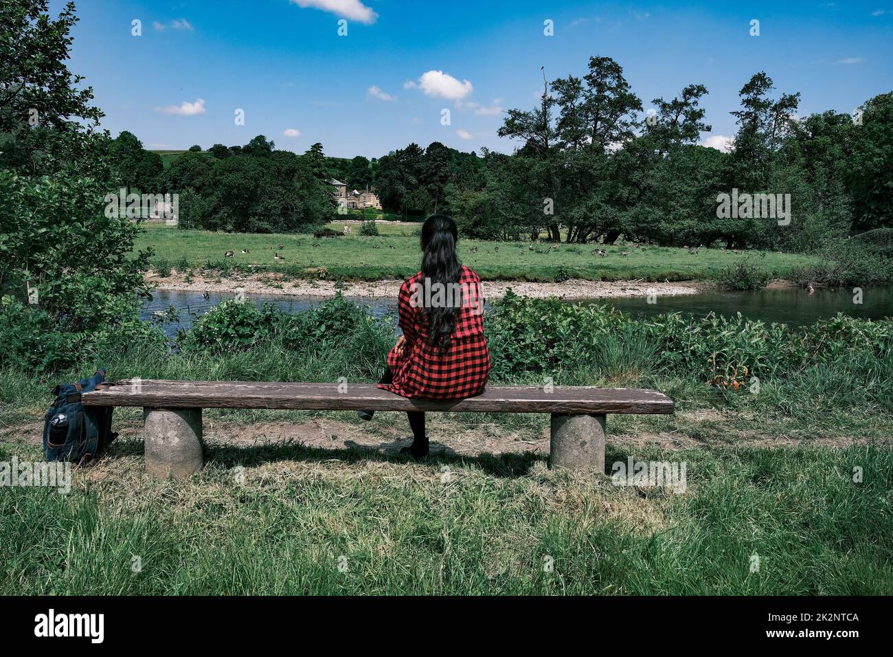 A girl with long hair sitting alone on a wooden bench and looking to a ...