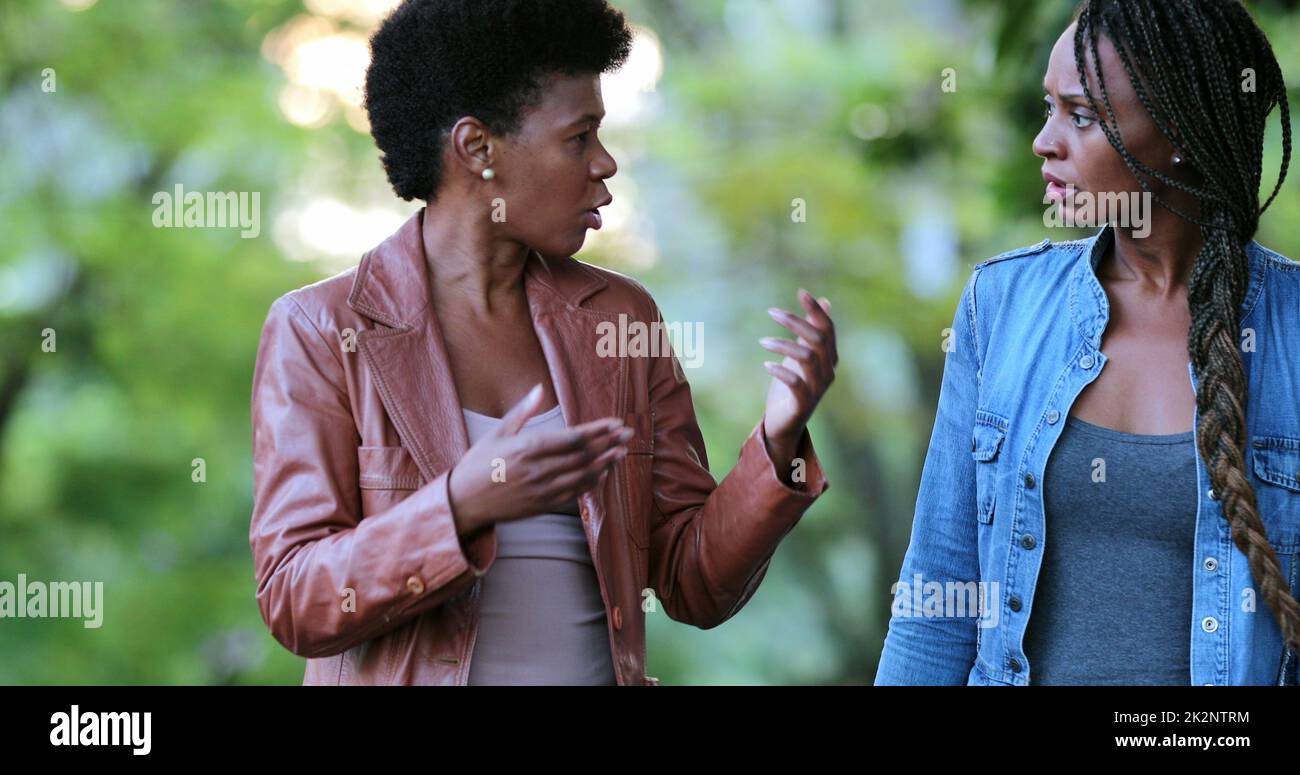 Two women talking outside while walking. African friends in ...
