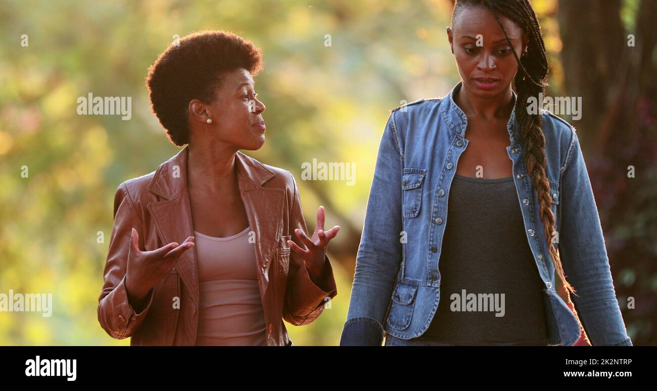 Two women talking outside while walking. African friends in ...