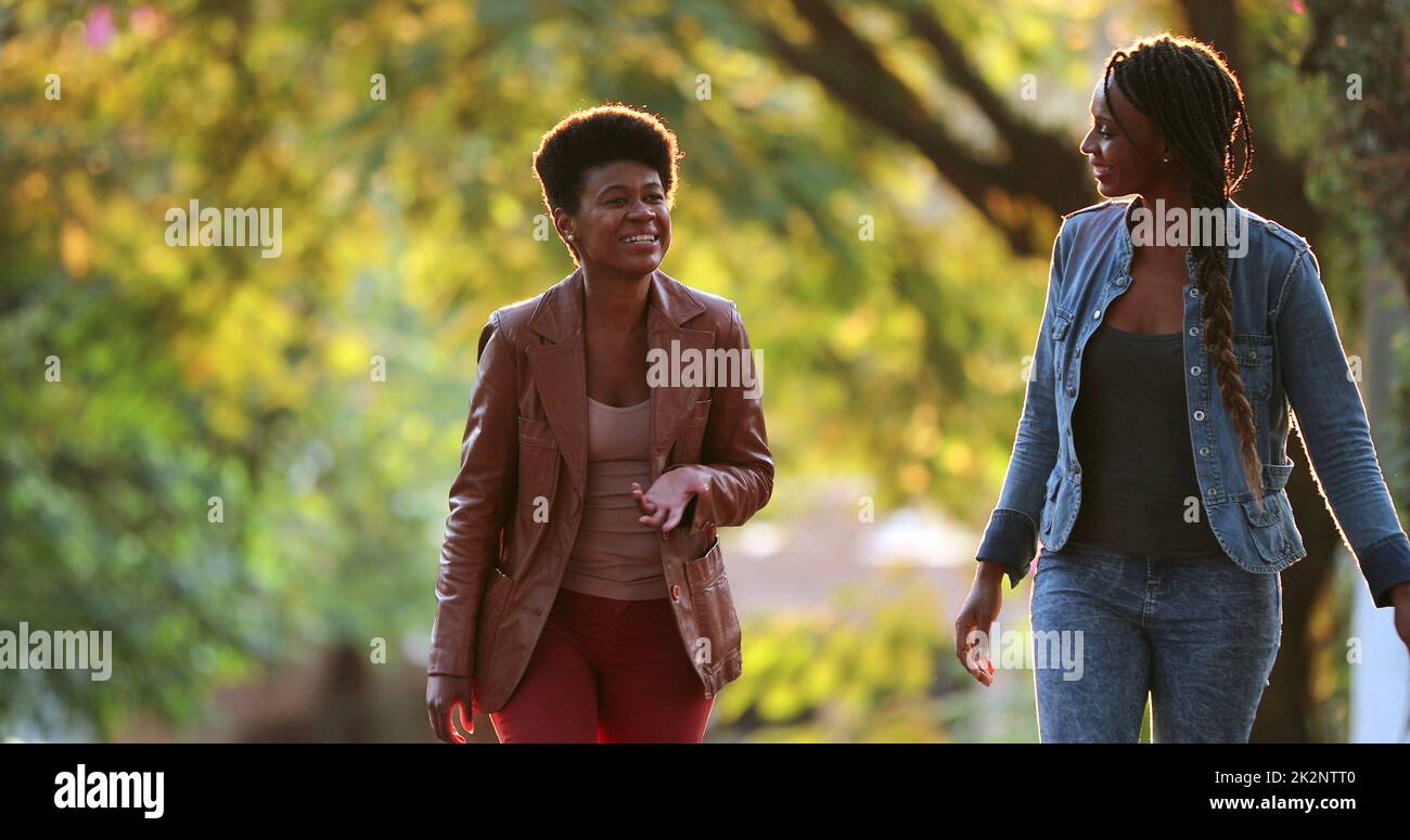 Two women talking outside while walking. African friends in ...
