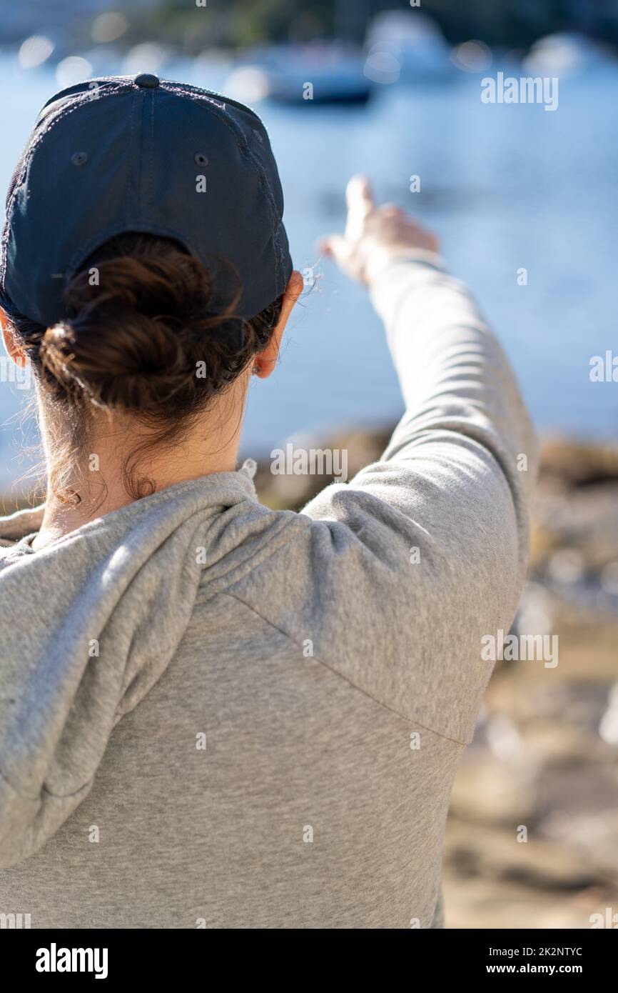 A vertical back view of a female with a bun and a blue cap pointing at ...