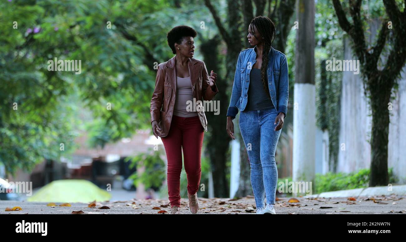 Two women talking outside while walking. African friends in ...