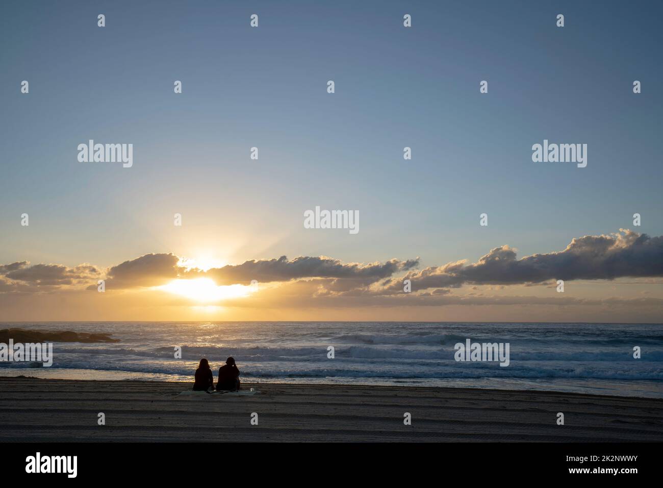A back view of a couple sitting on the sandy beach watching the sea ...