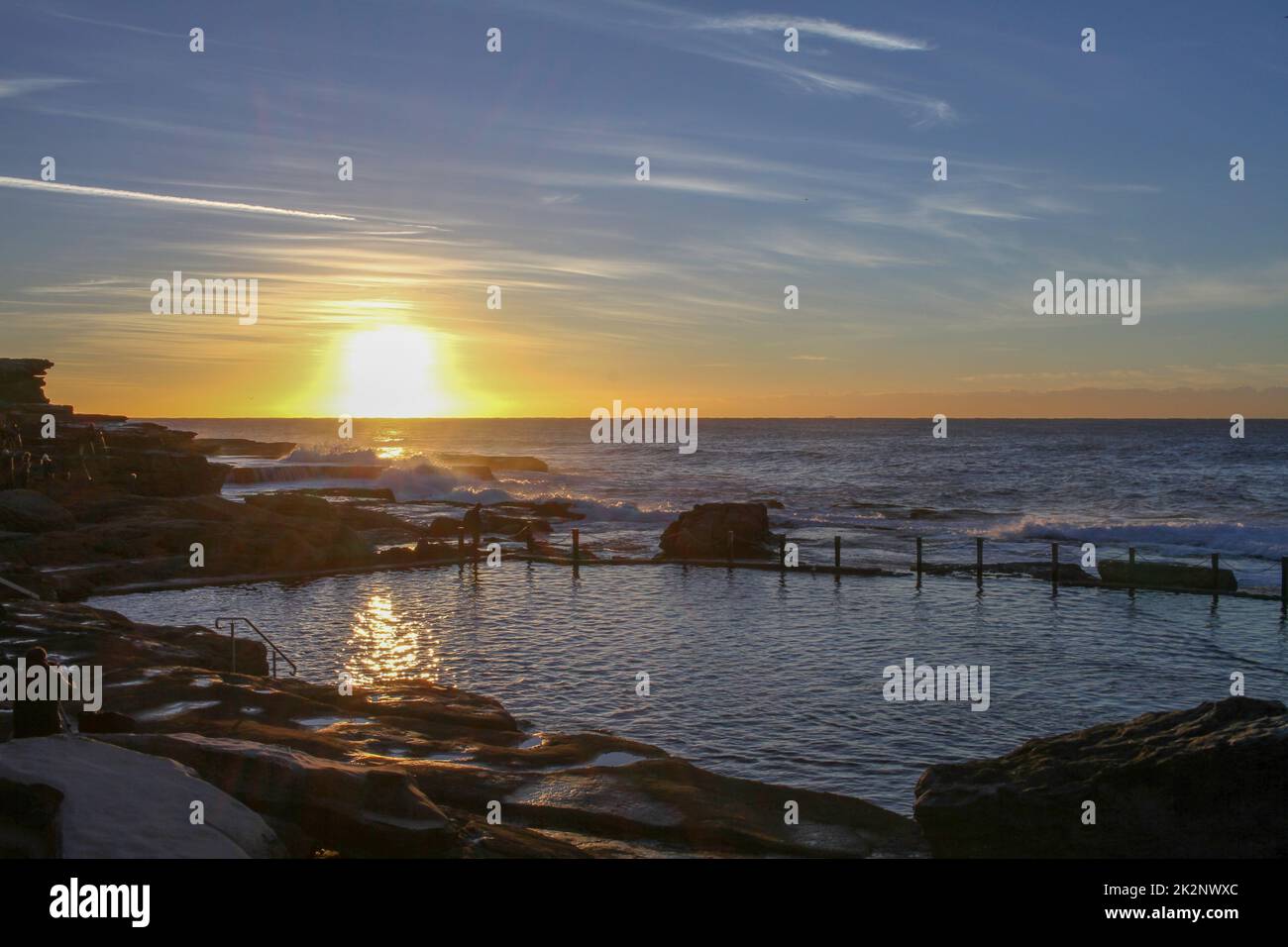 The bright sun shining behind clouds in the blue sunset sky over the ...