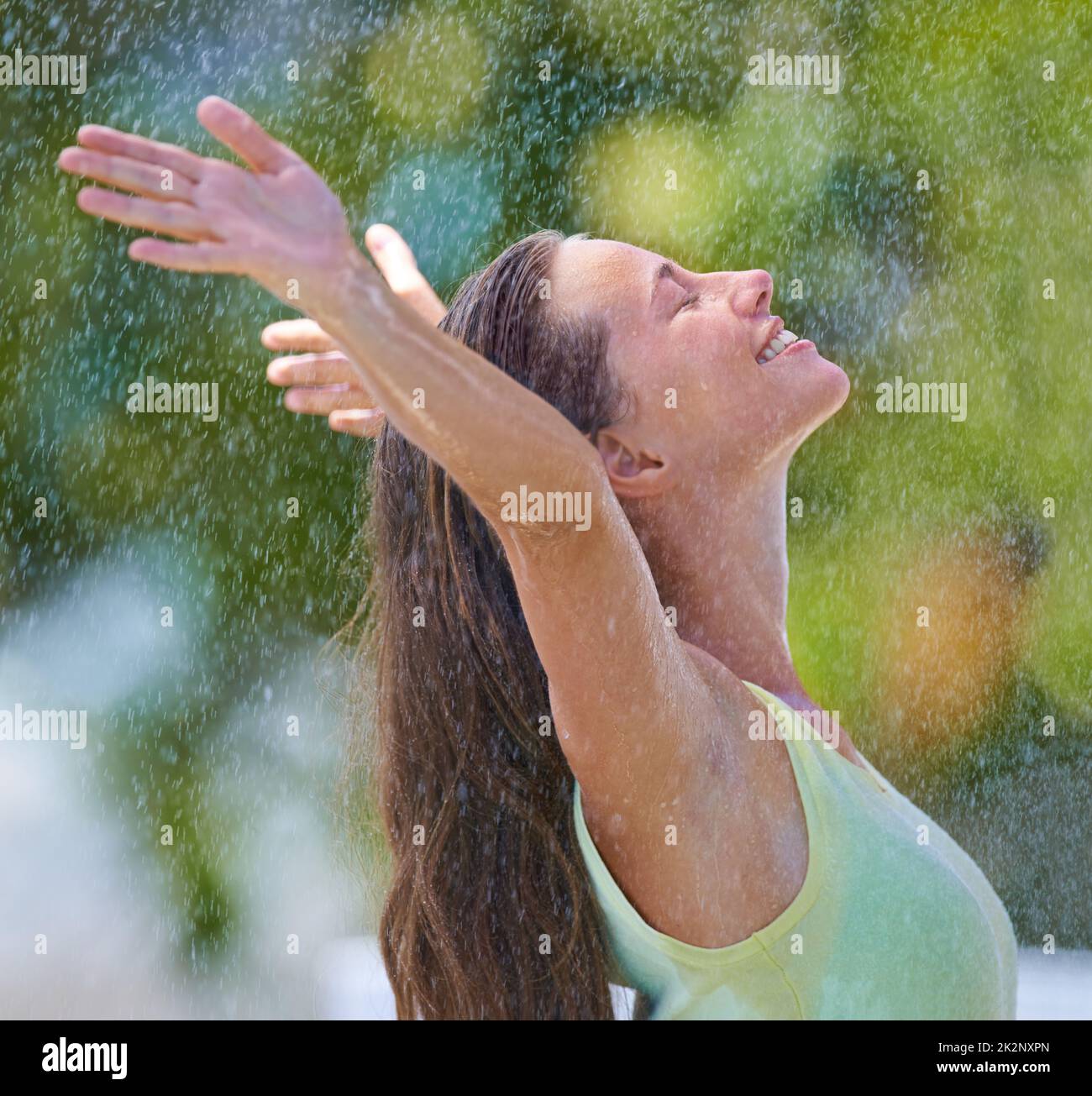 I feel alive. Side view of a young woman standing happily in the rain ...