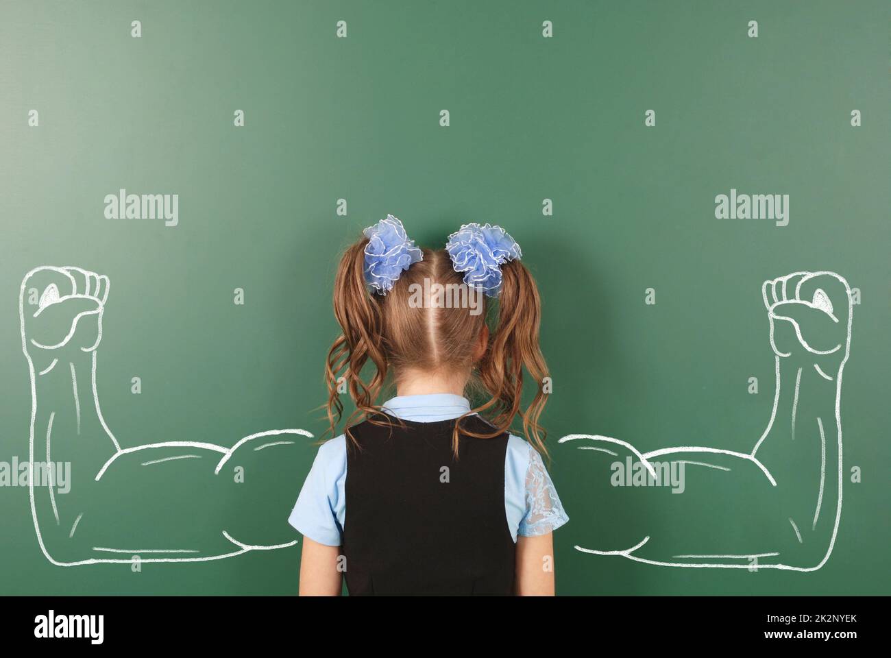 Cute schoolgirl over green board background with strong arms drawing ...