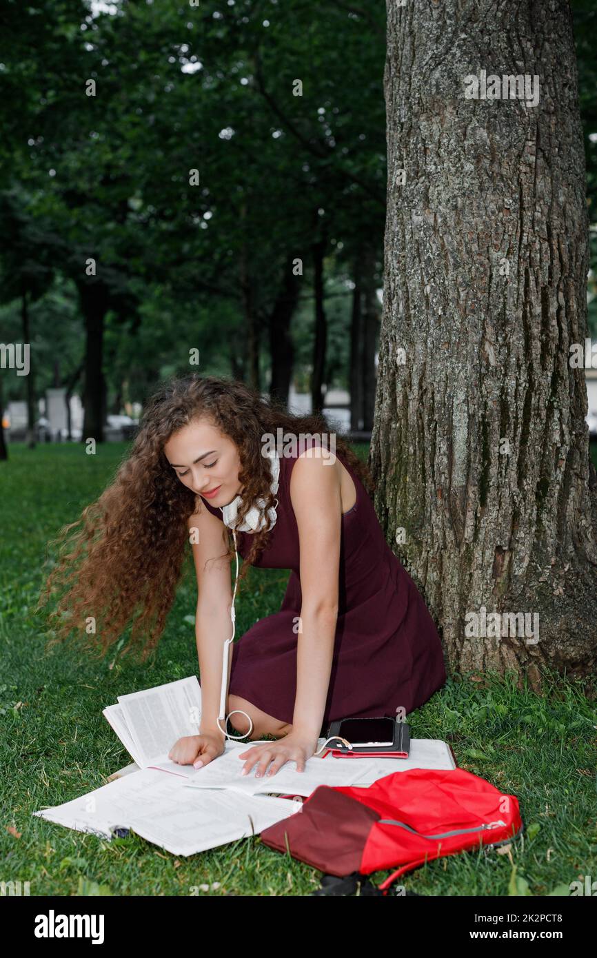 girl student holding book and sitting under tree Stock Photo - Alamy