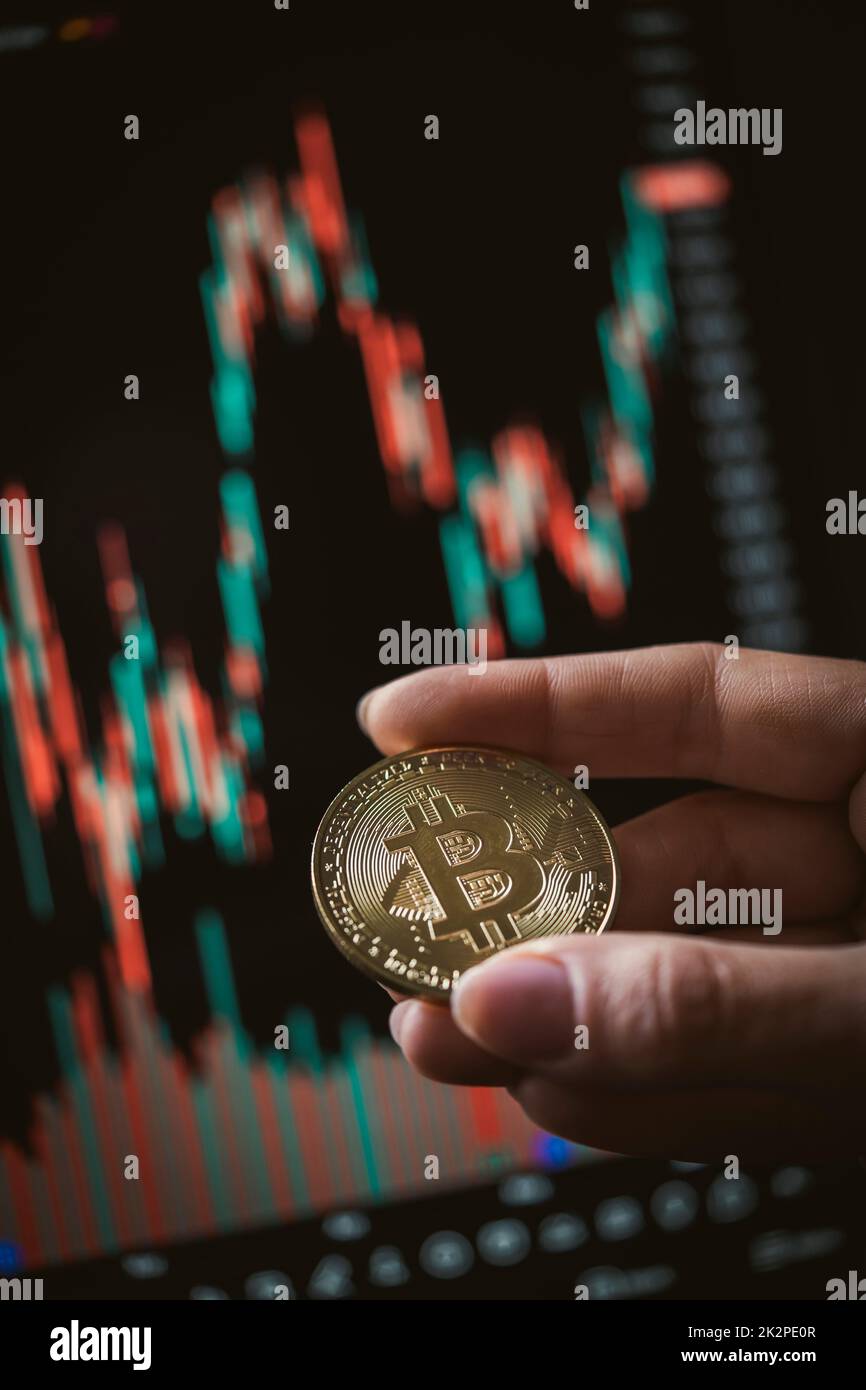 Hand holding a gold Bitcoin coin with candle stick graph chart and ...