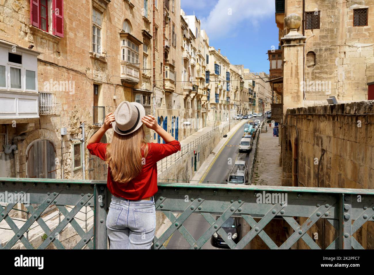 Tourist woman holds hat on iron bridge looking the old town of Valletta ...