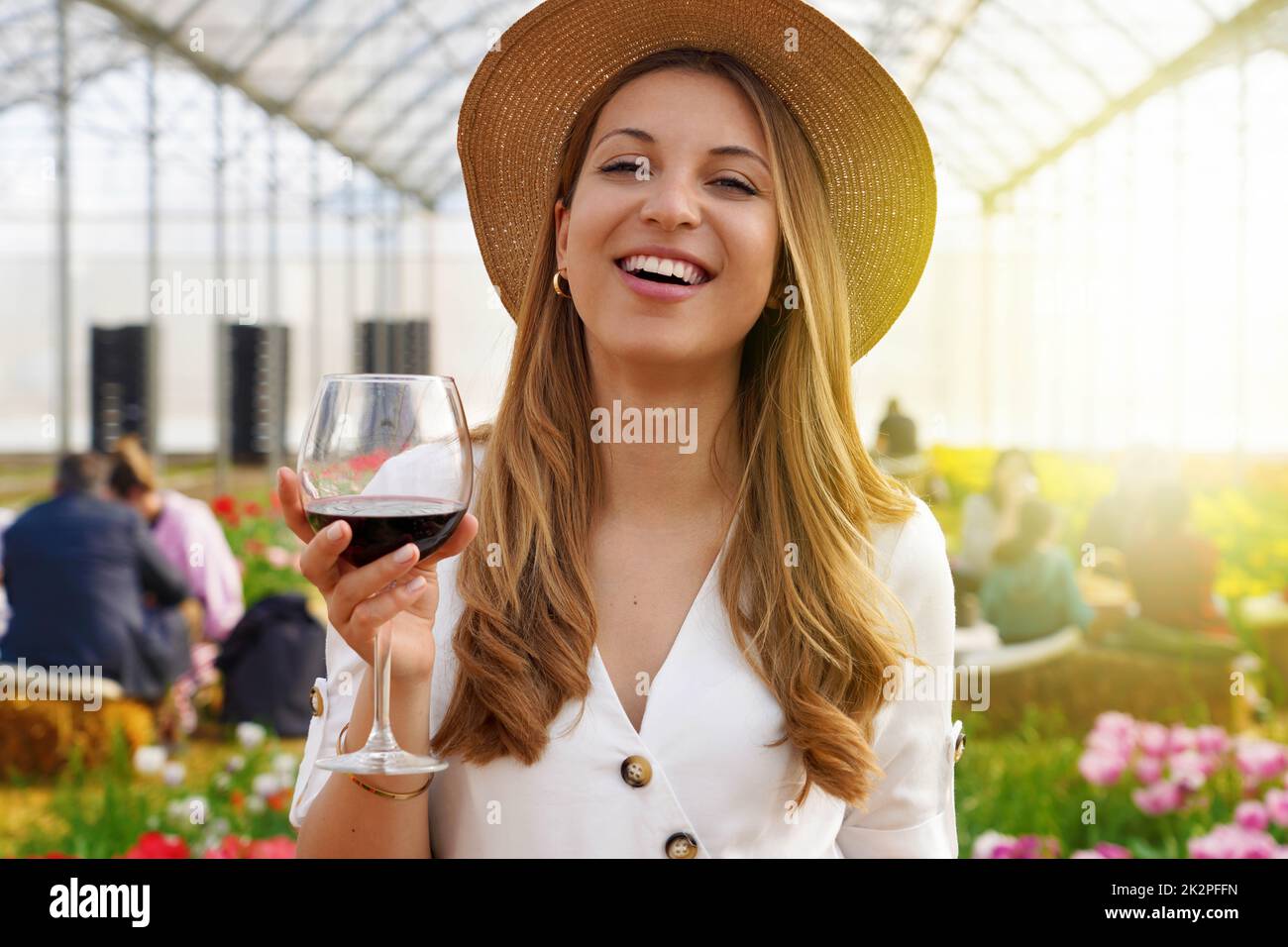 Woman looking at camera and holding glass of wine with people among ...
